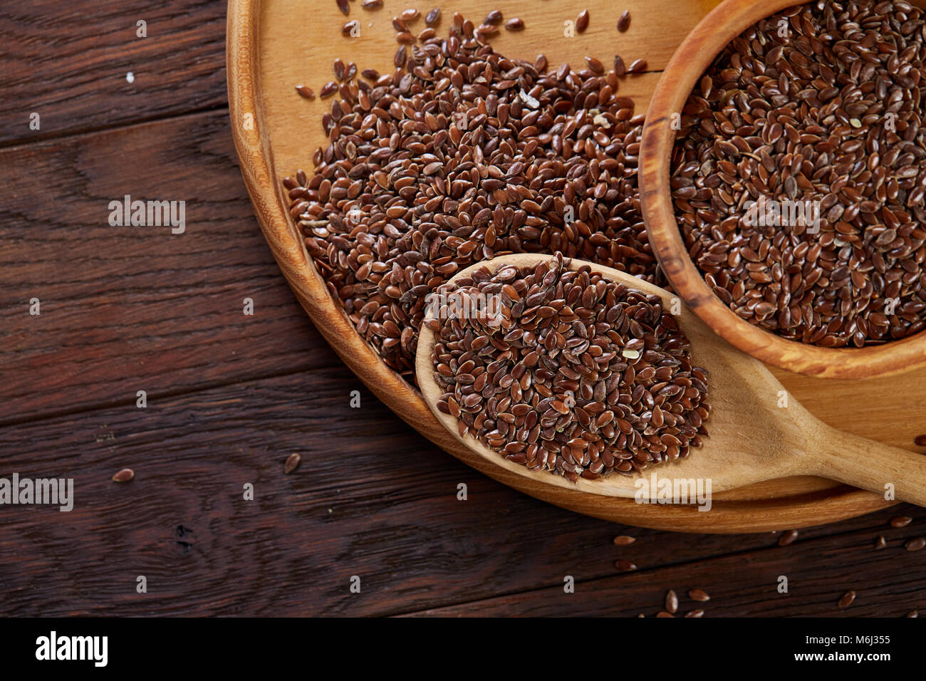 Top view close-up picture of flax seeds in wooden bowl and spoon isolated on brown rustic wooden ...