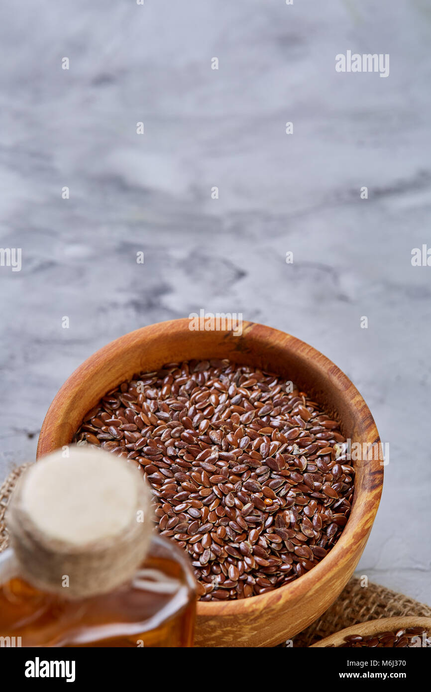 Brown flax seeds in wooden plate and flaxseed oil in glass bottle on brown rustic wooden ...