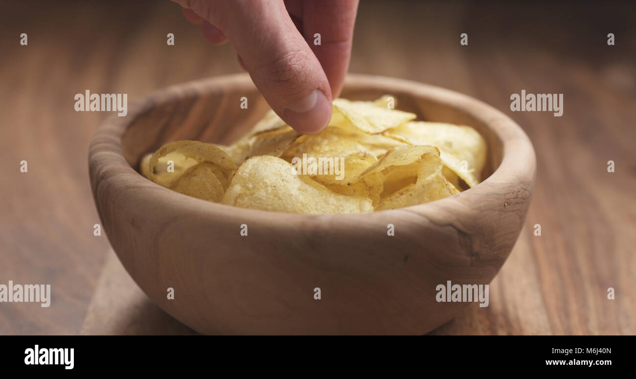 closeup man hand take potato chip from wood bowl Stock Photo - Alamy