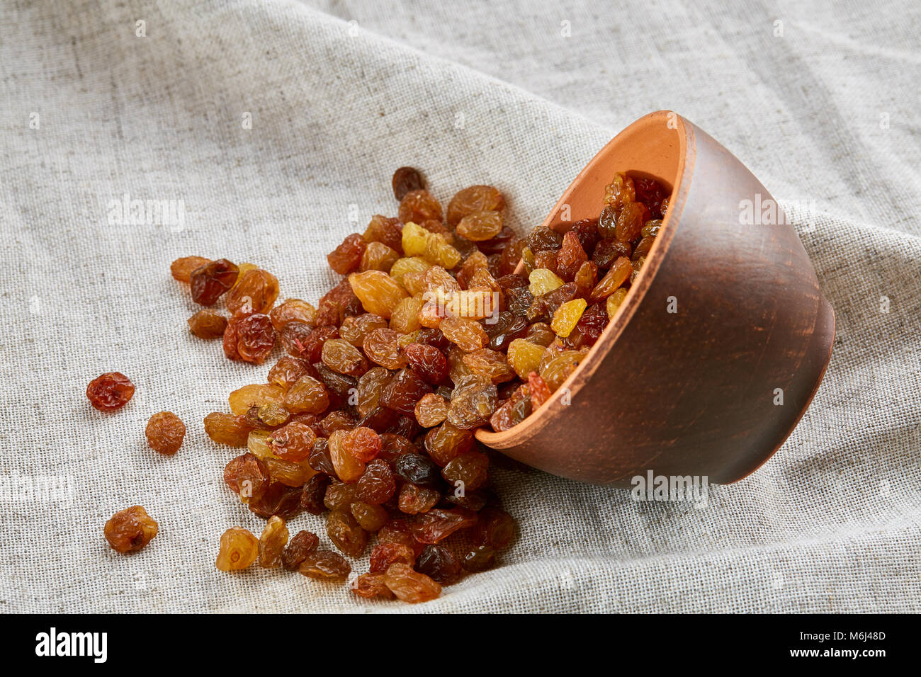 Close-up picture of wooden bowl with golden raisins on light grey ...