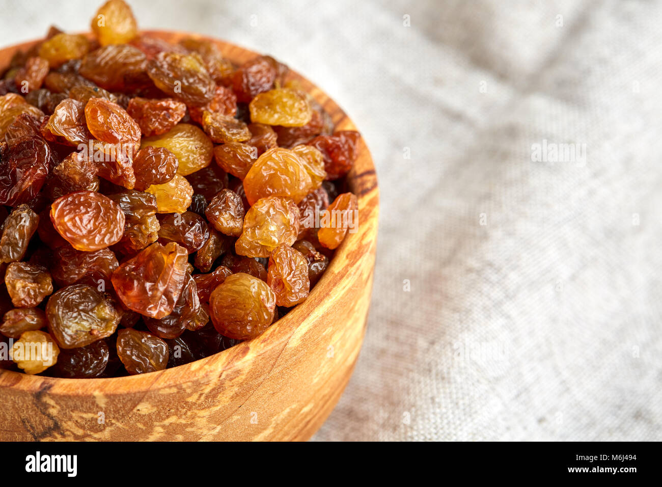 Close-up picture of wooden bowl with golden raisins on light grey ...