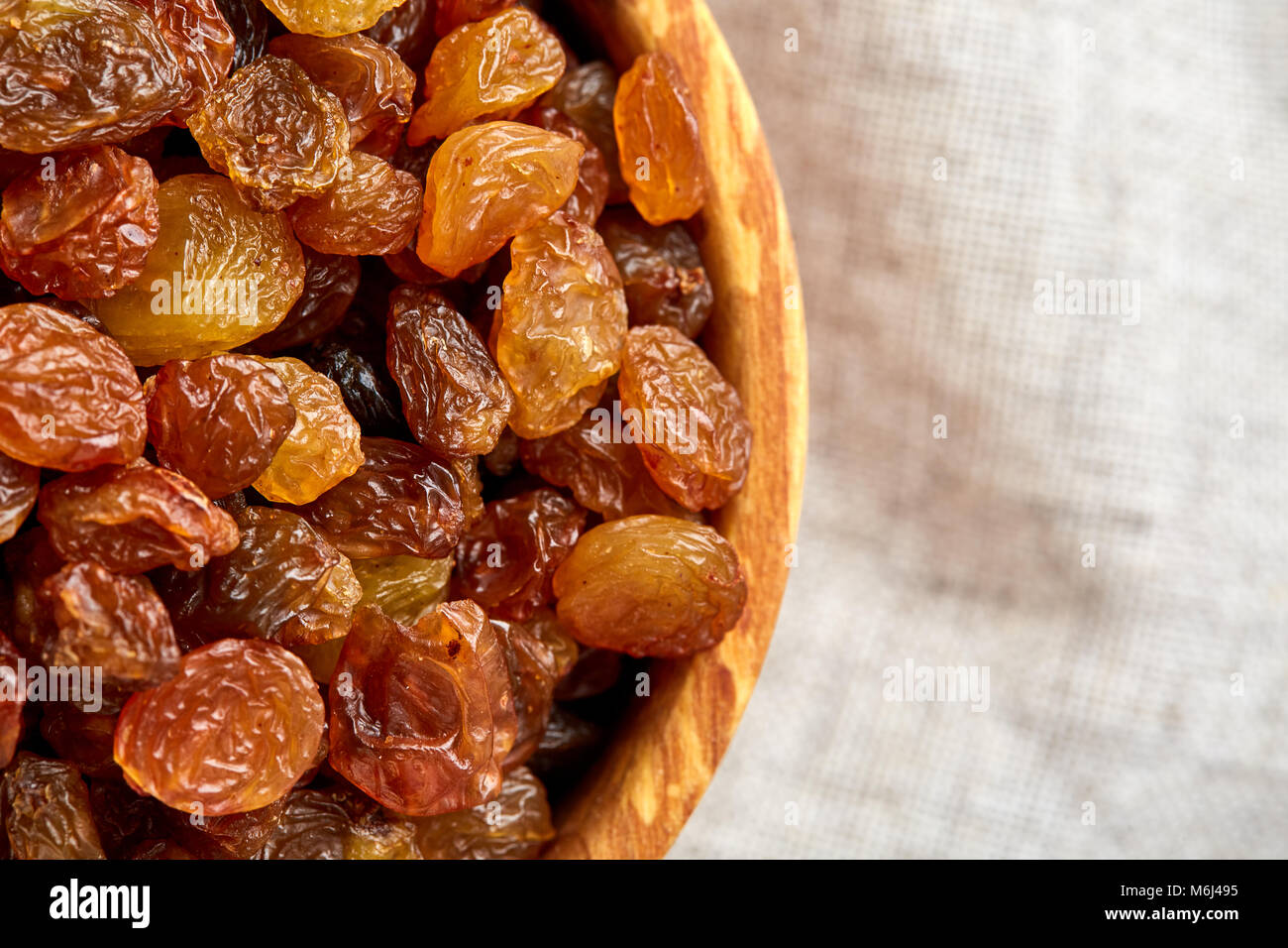Close-up picture of wooden bowl with golden raisins on light grey ...