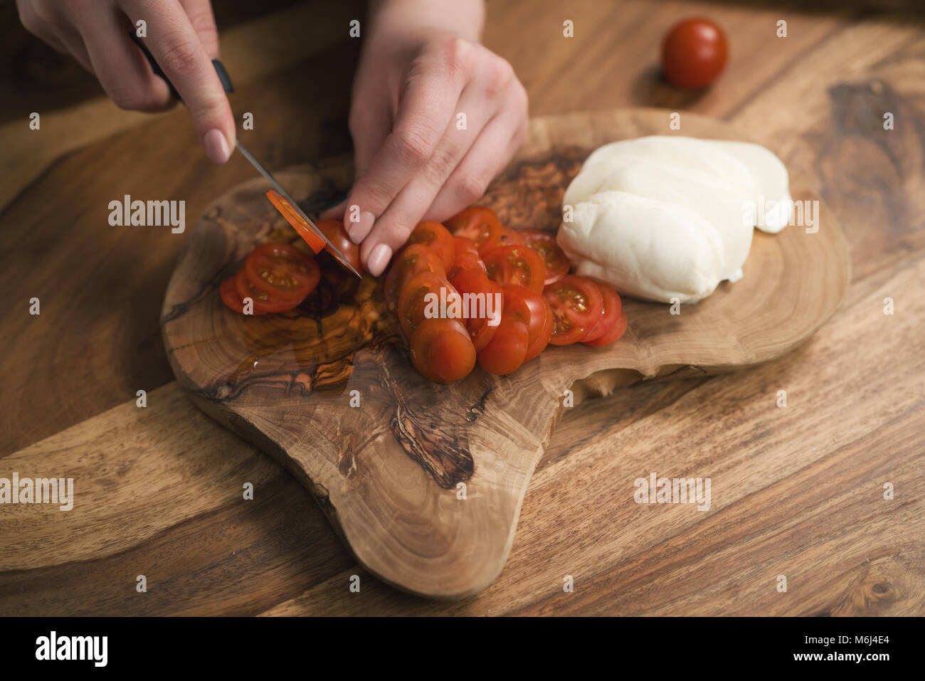 female teen hand slicing cherry tomatoes with knife on wooden board ...