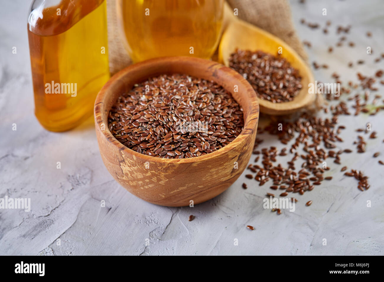Flax seeds in bowl, wooden scoop and flaxseed oil in glass bottle over light textured background ...