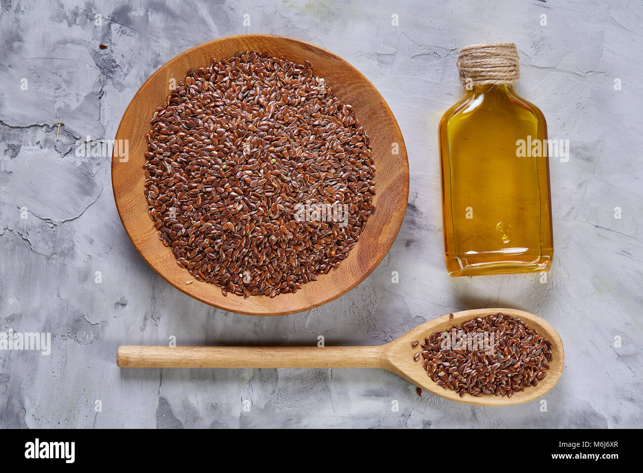 Flax seeds in bowl, wooden scoop and flaxseed oil in glass bottle over light textured background ...