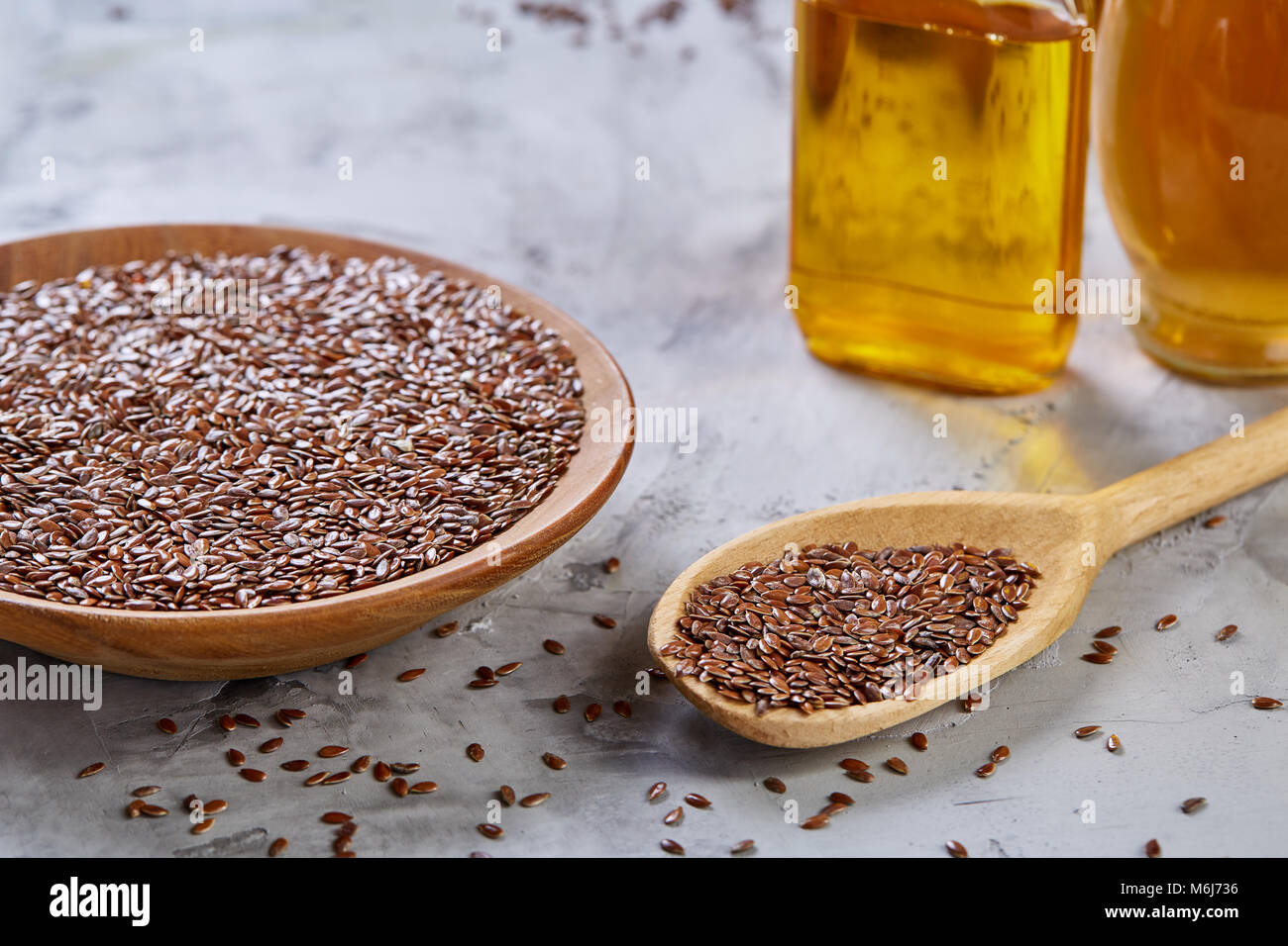 Flax seeds in bowl, wooden scoop and flaxseed oil in glass bottle over light textured background ...