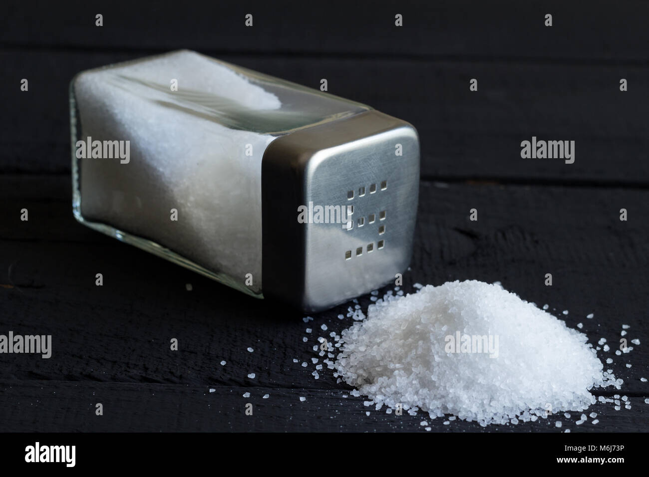 Glass salt shaker on black rustic table and heap of salt crystals with ...
