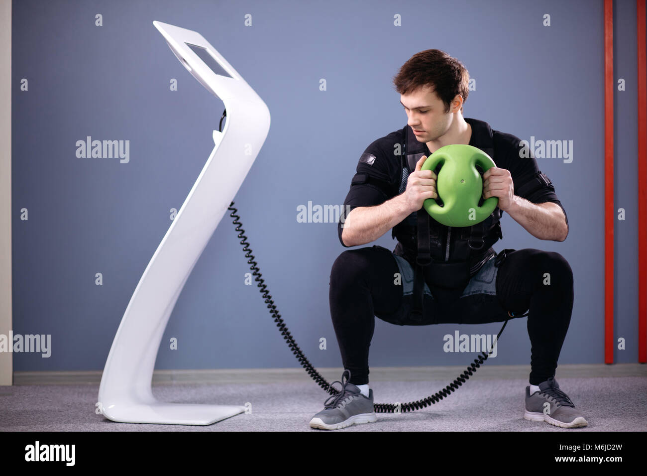 Man in electric muscular suit to stimulate with training medecine ball ...