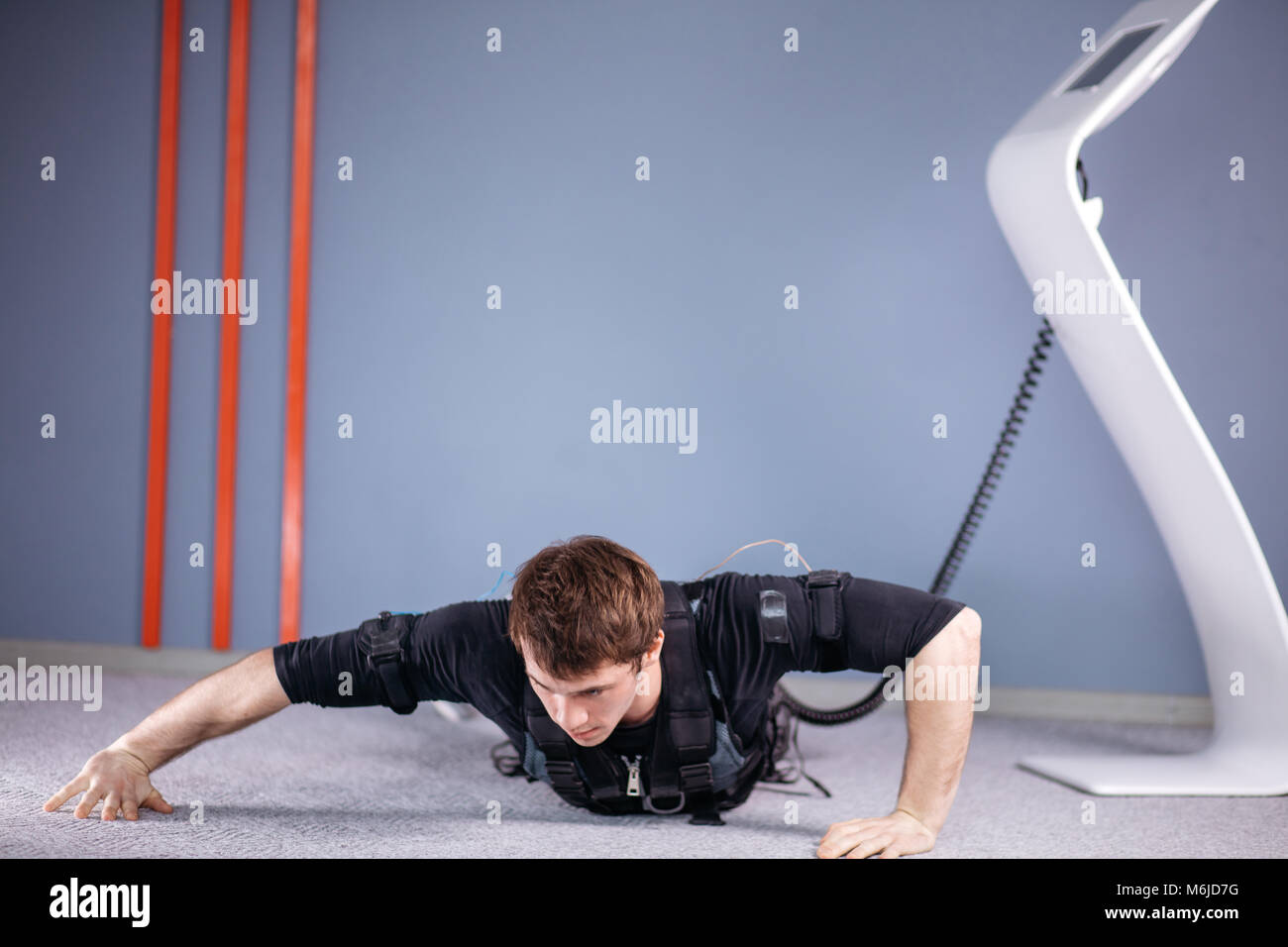 EMS male doing push ups in gym while connected to electric muscle ...