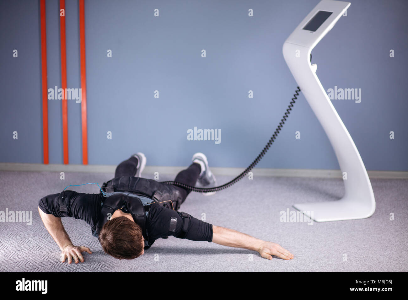 EMS male doing push ups in gym while connected to electric muscle ...