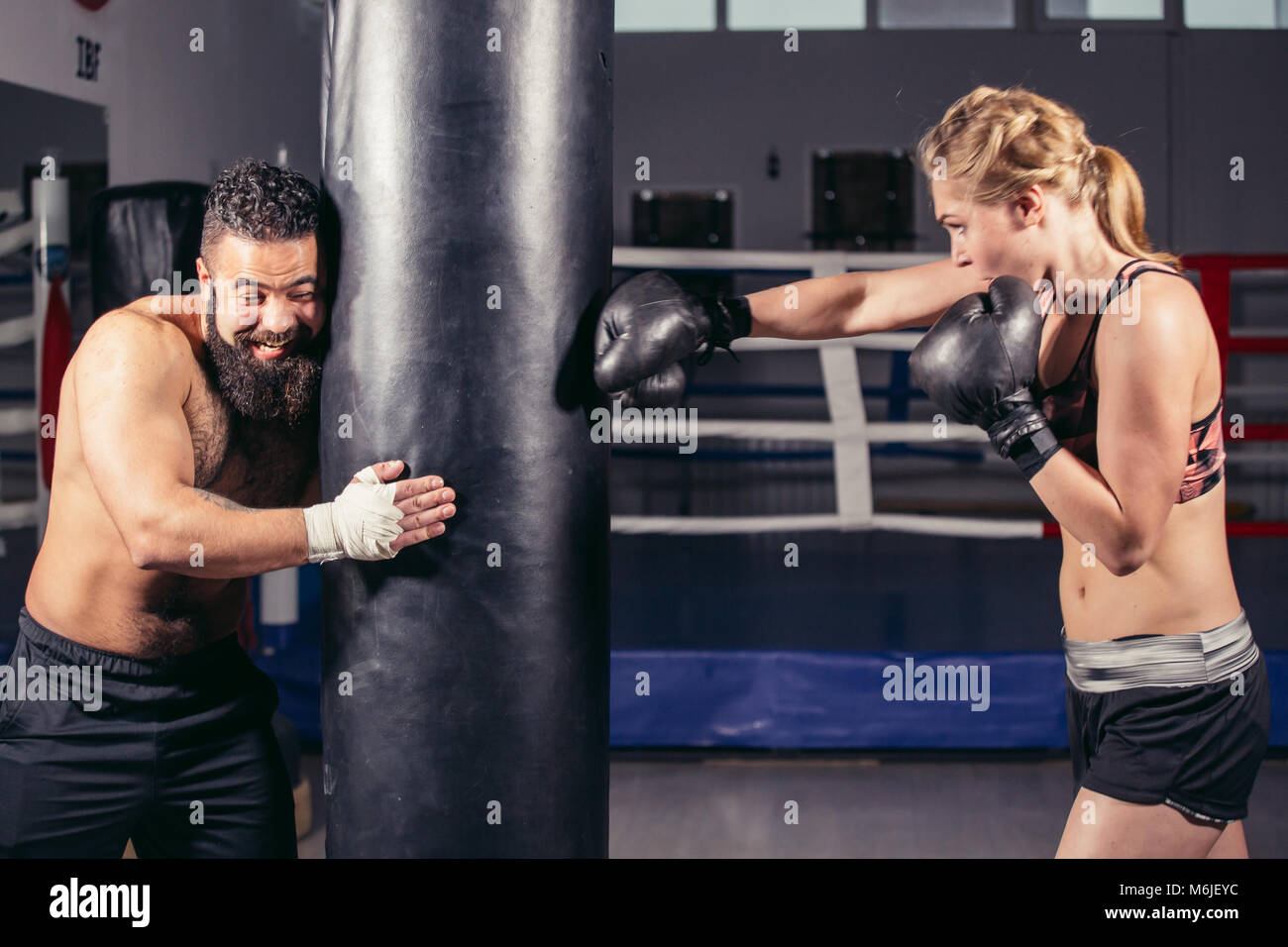 woman working out with boxing gloves and punching bag with her trainer ...