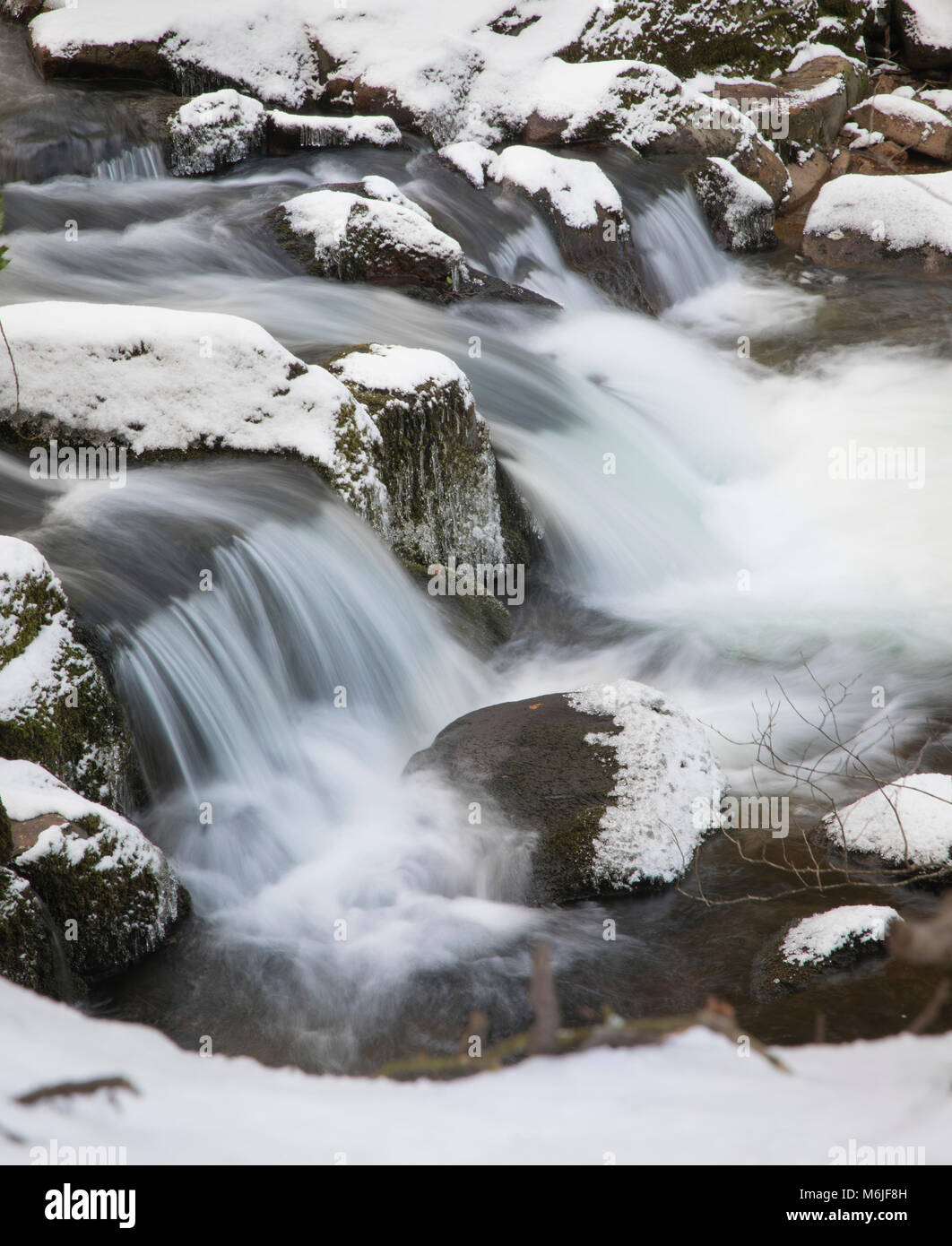 Long Exposure of water flowing down a stream surrounded by snow, River ...