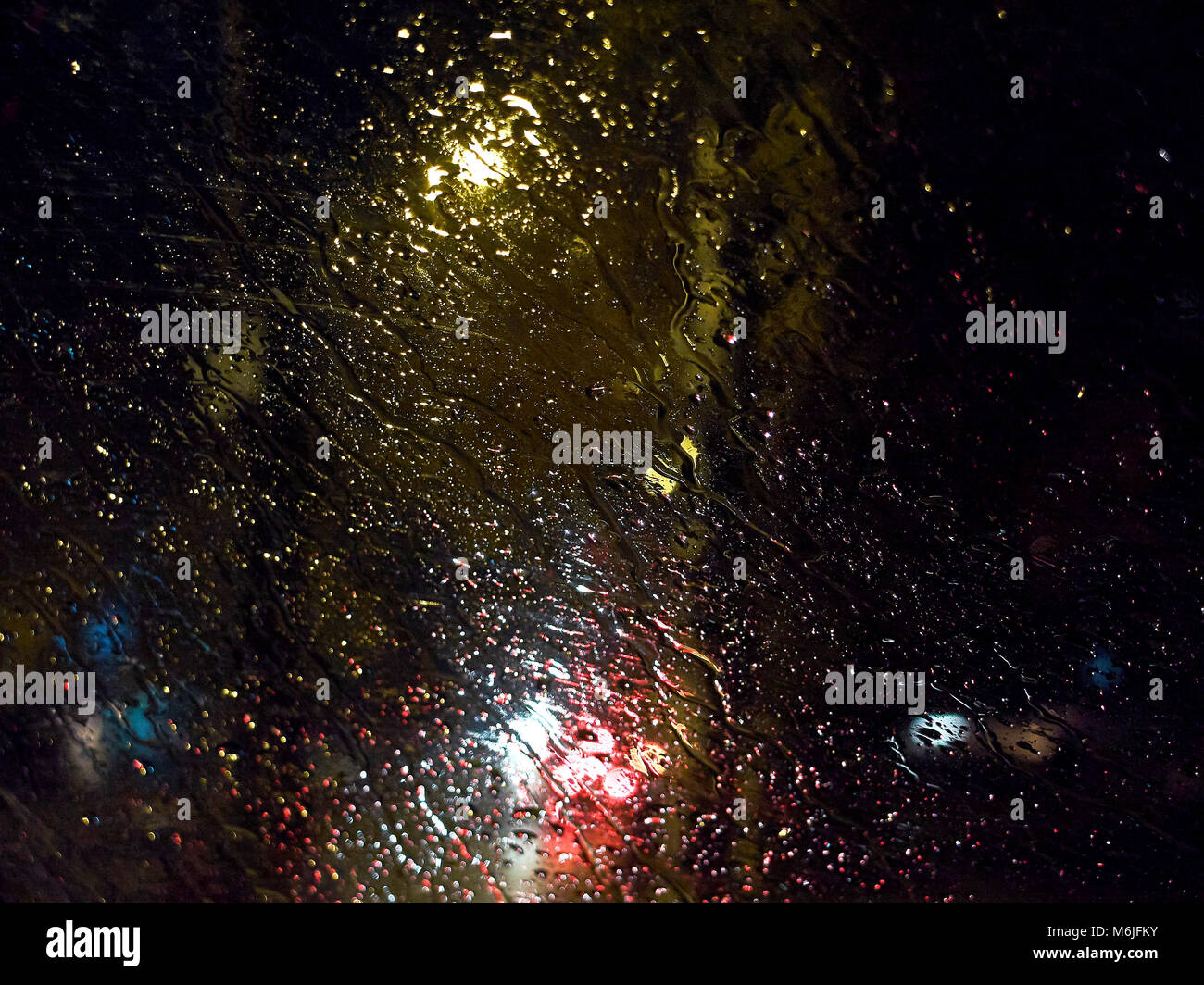 Raindrops on the car window at night illuminated by street lights ...