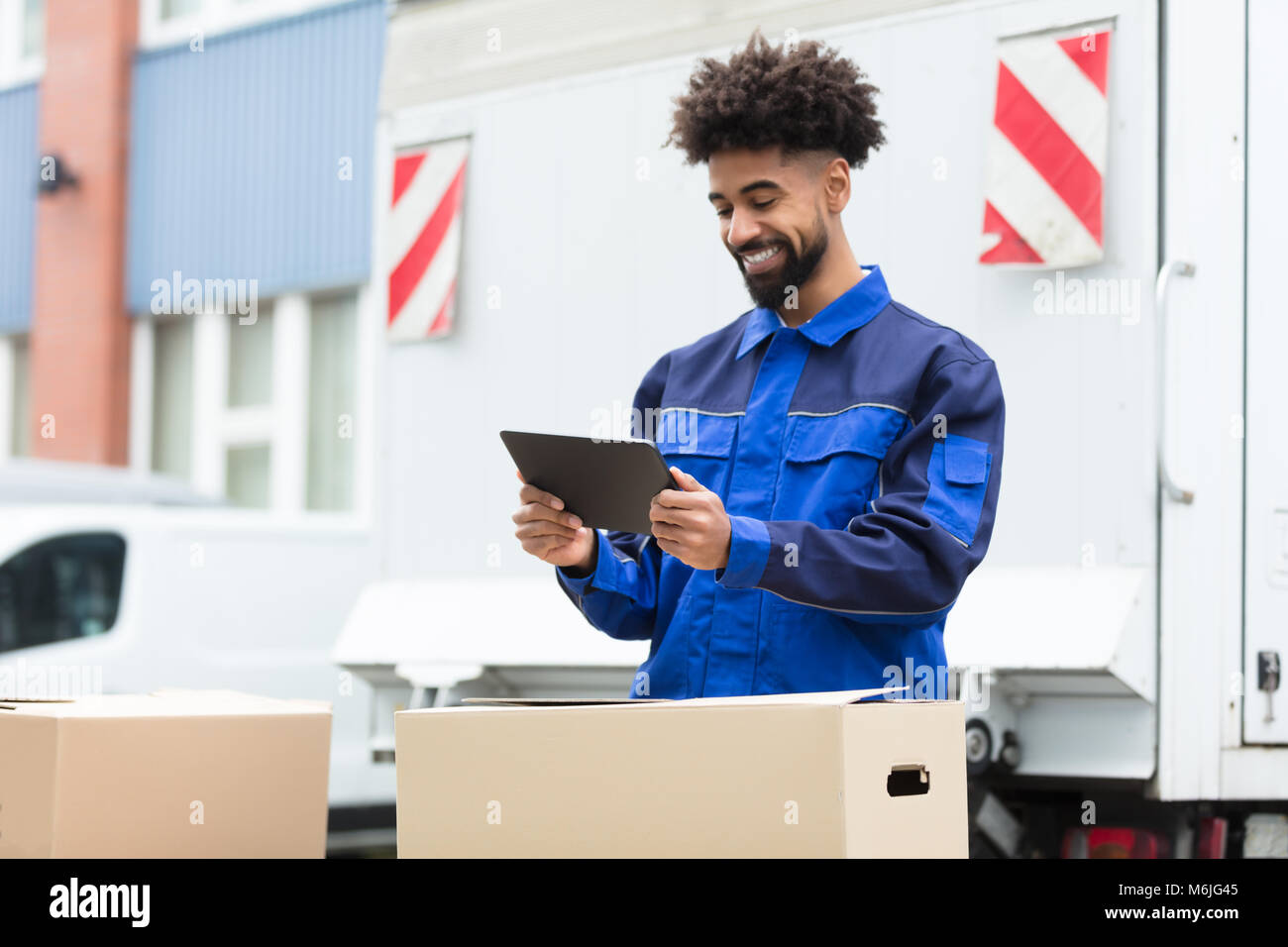 Smiling Delivery Man Standing Near The Van Checking His Order On ...