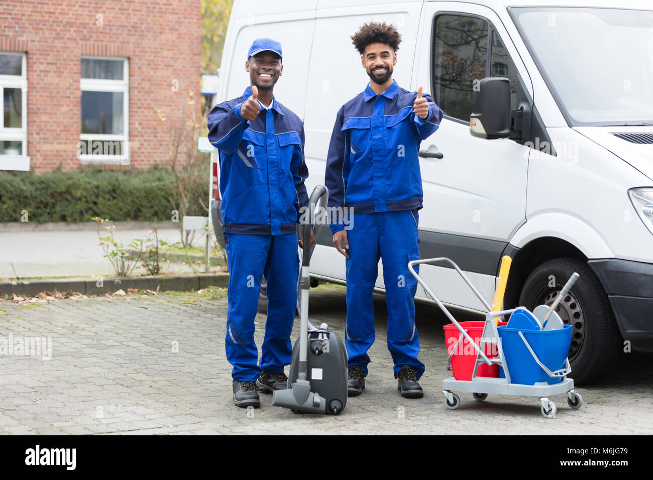 Portrait Of Two Happy Male Janitor Standing With Cleaning Equipment ...