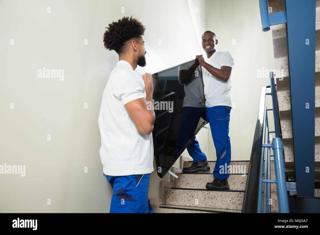 Close-up Of Two Male Young Movers Carrying Television While Climbing ...