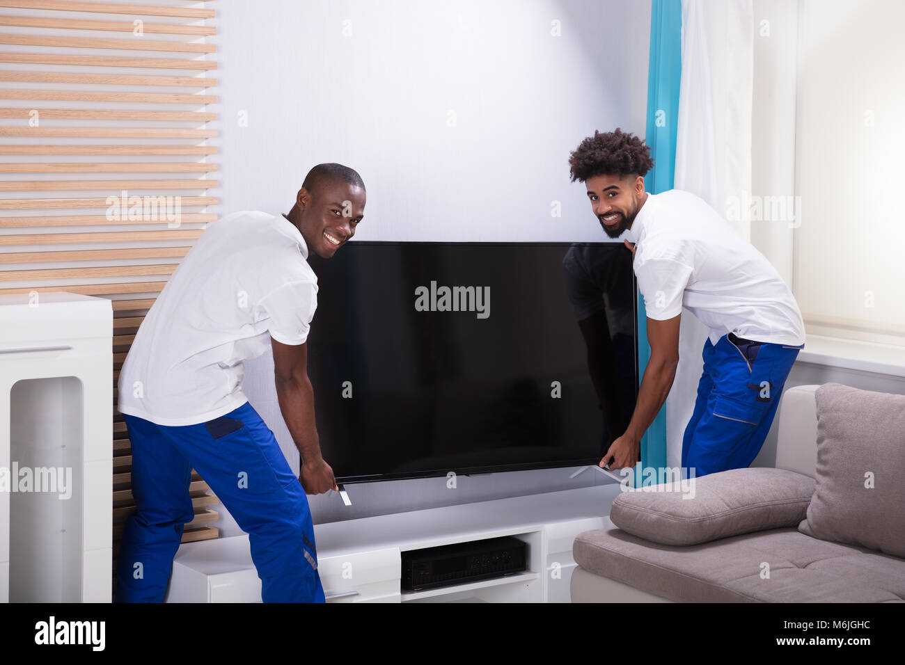 Portrait Of Two Smiling Young Male Movers Placing The Television In The ...