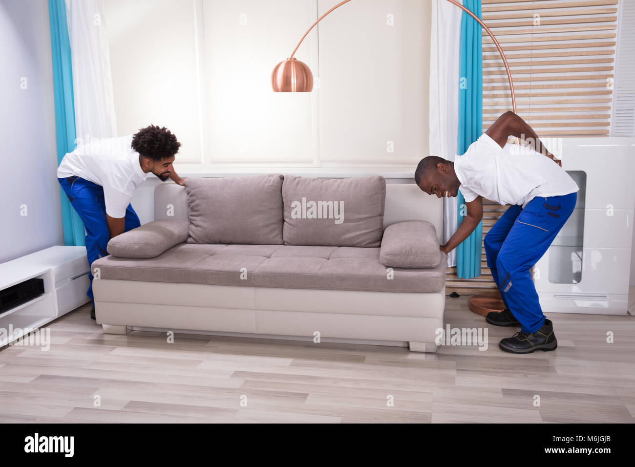 Young Male Movers With Backache Lifting Couch In The Living Room Stock ...