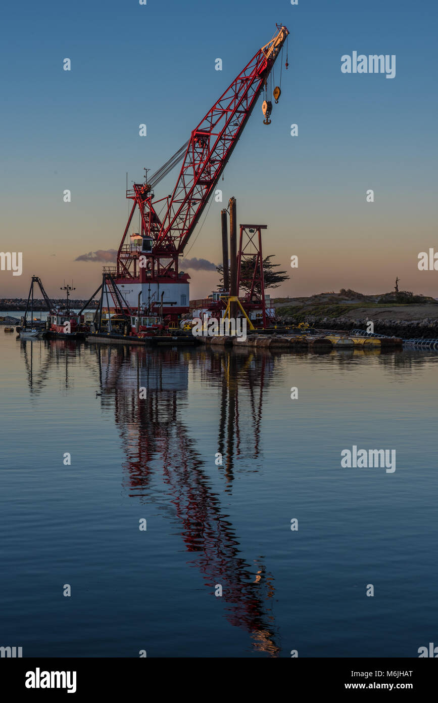 Marine floating crane reflected in calm water of the cove in the early ...