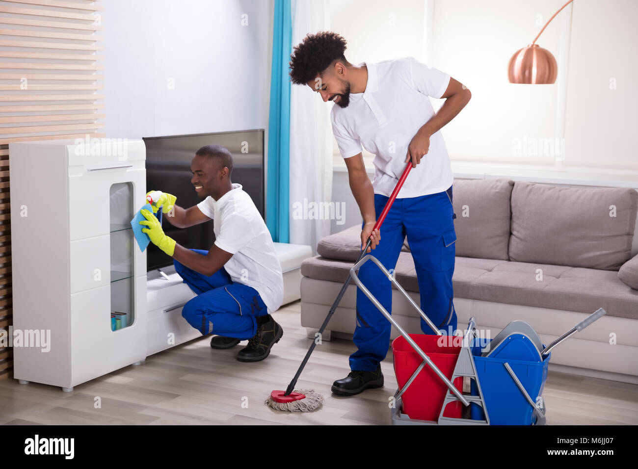 Two Smiling Young Male Janitor Cleaning The Cabinet And Mopping Floor ...