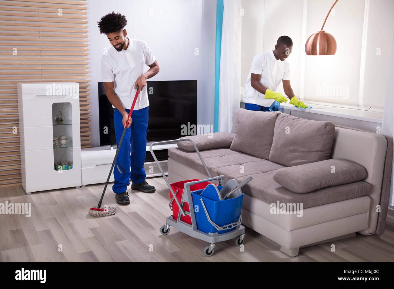 Two Smiling Young Male Janitor Cleaning The Windowsill And Mopping ...