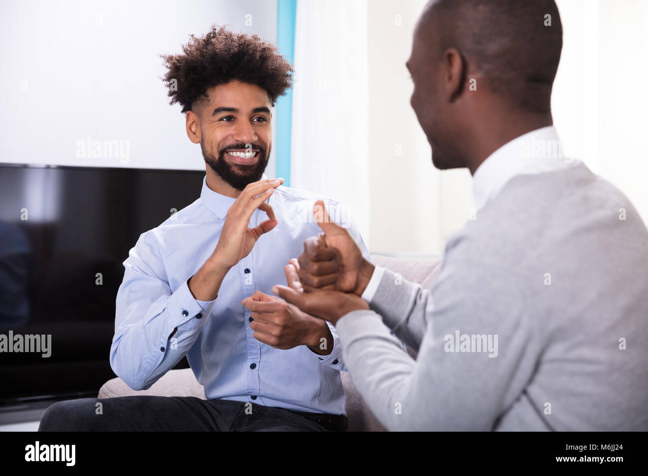 Two Young Happy Men Sitting On The Sofa Making Sign Languages Stock ...