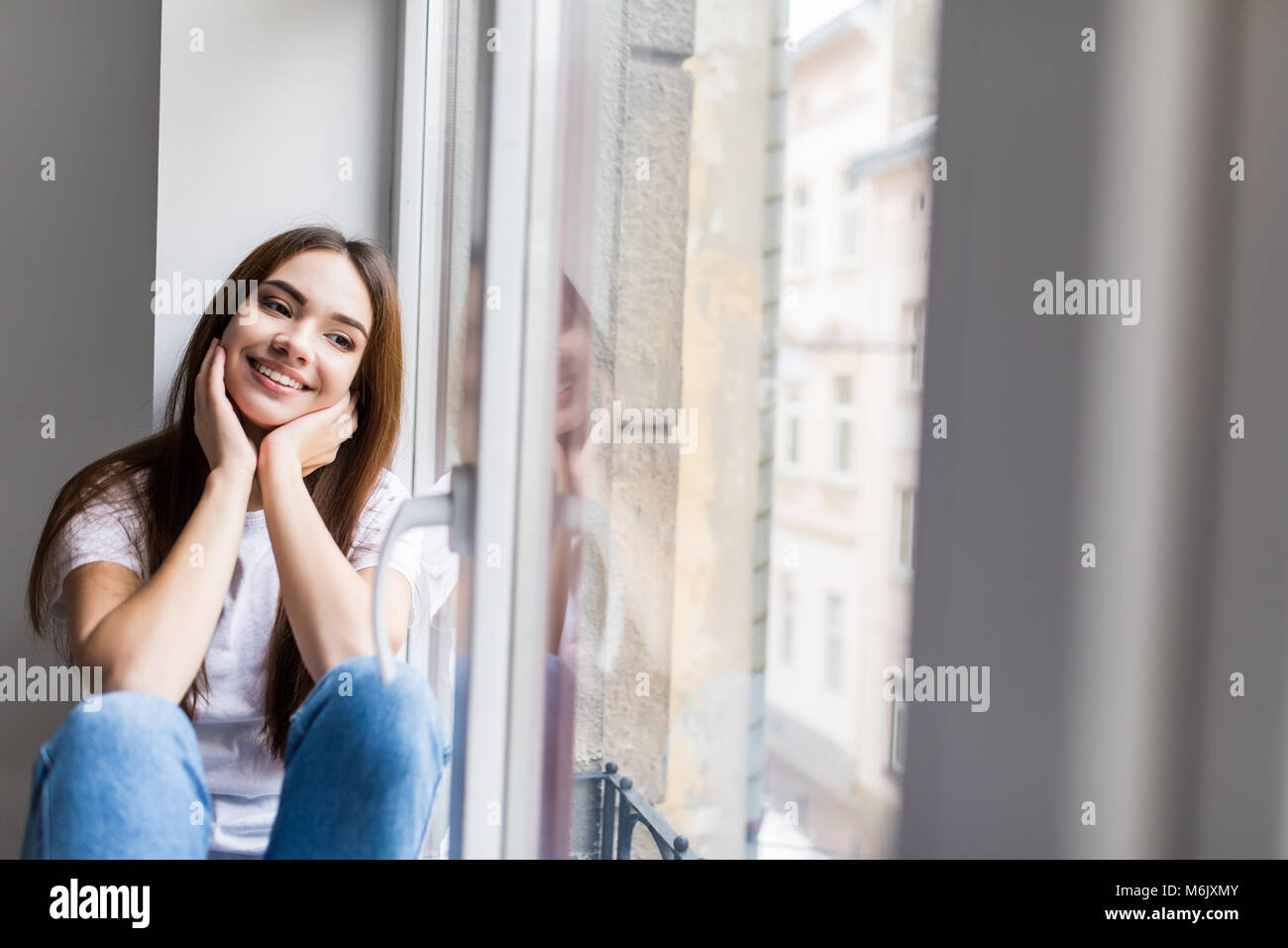 Beautiful smiling woman sitting on windowsill and smile Stock Photo - Alamy