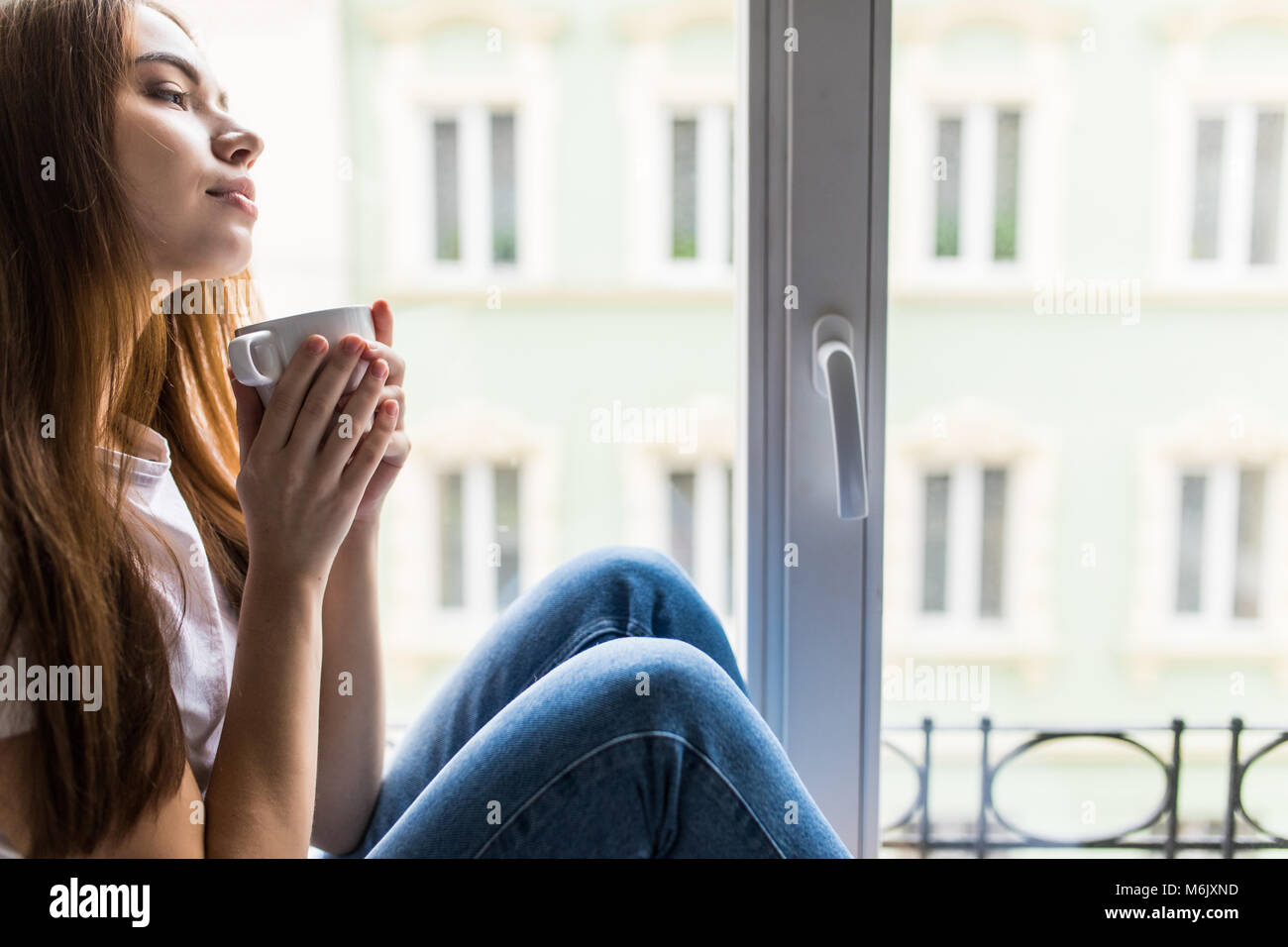 Beautiful woman drinking coffee and looking through window while ...