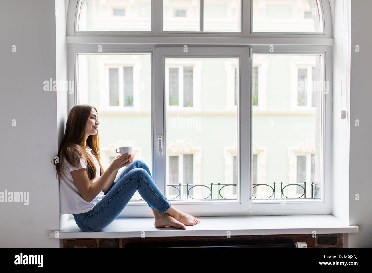 Beautiful woman drinking coffee and looking through window while ...