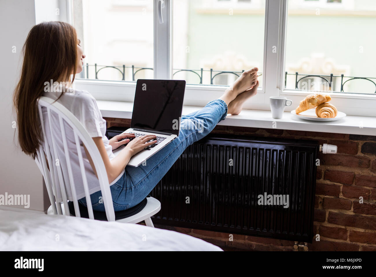 Relaxed Woman working laptop with legs on widnowsill with morning ...
