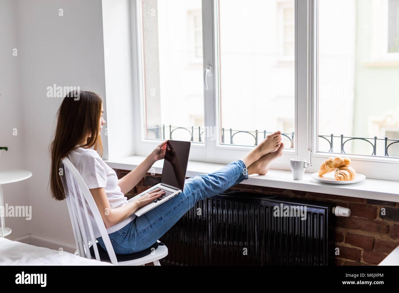Relaxed Woman working laptop with legs on widnowsill with morning ...
