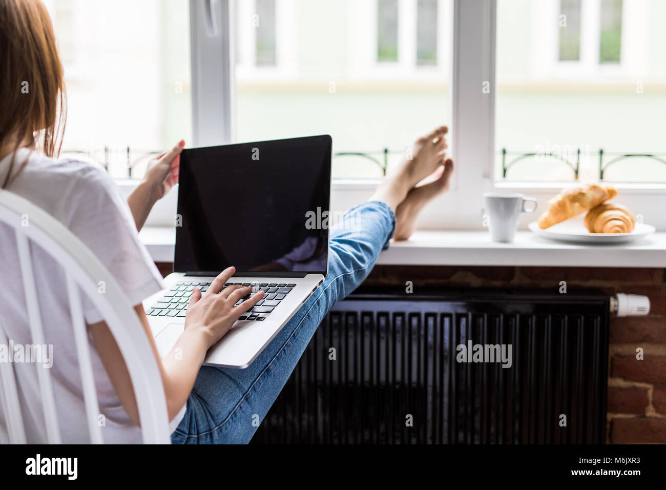 Relaxed Woman working laptop with legs on widnowsill with morning ...