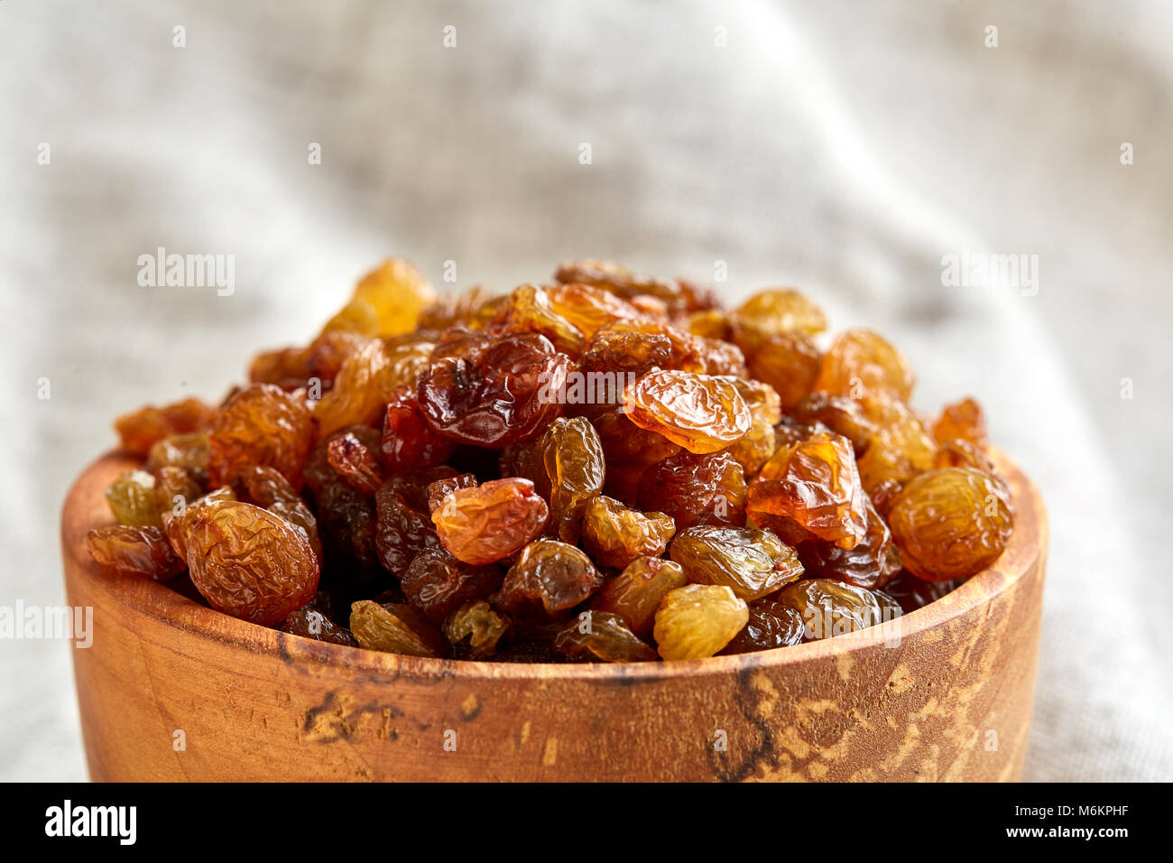 Close-up picture of wooden bowl with golden raisins on light grey ...