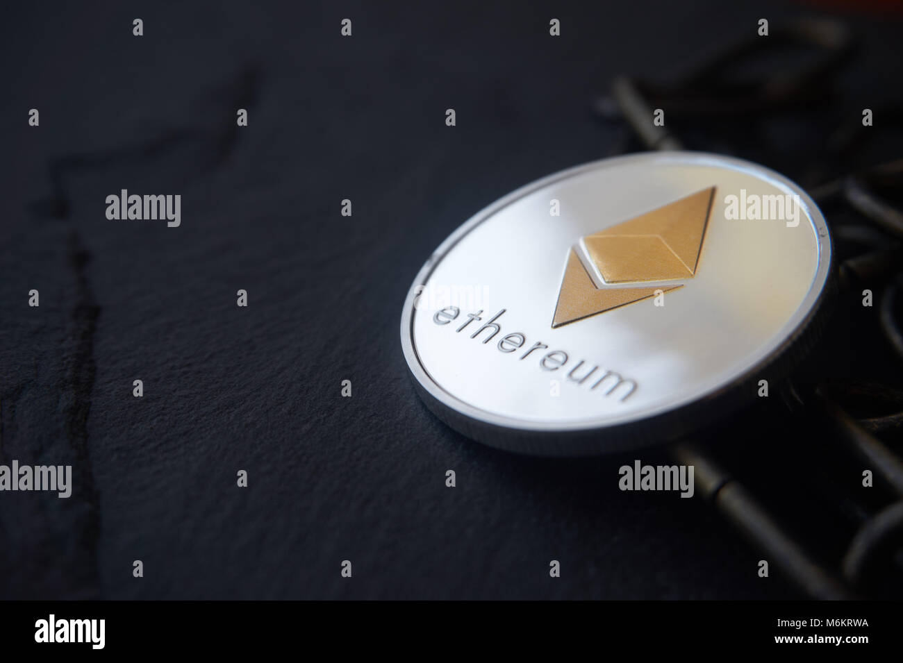 Silver Ethereum coin lying on the grey stone and copper chain ...