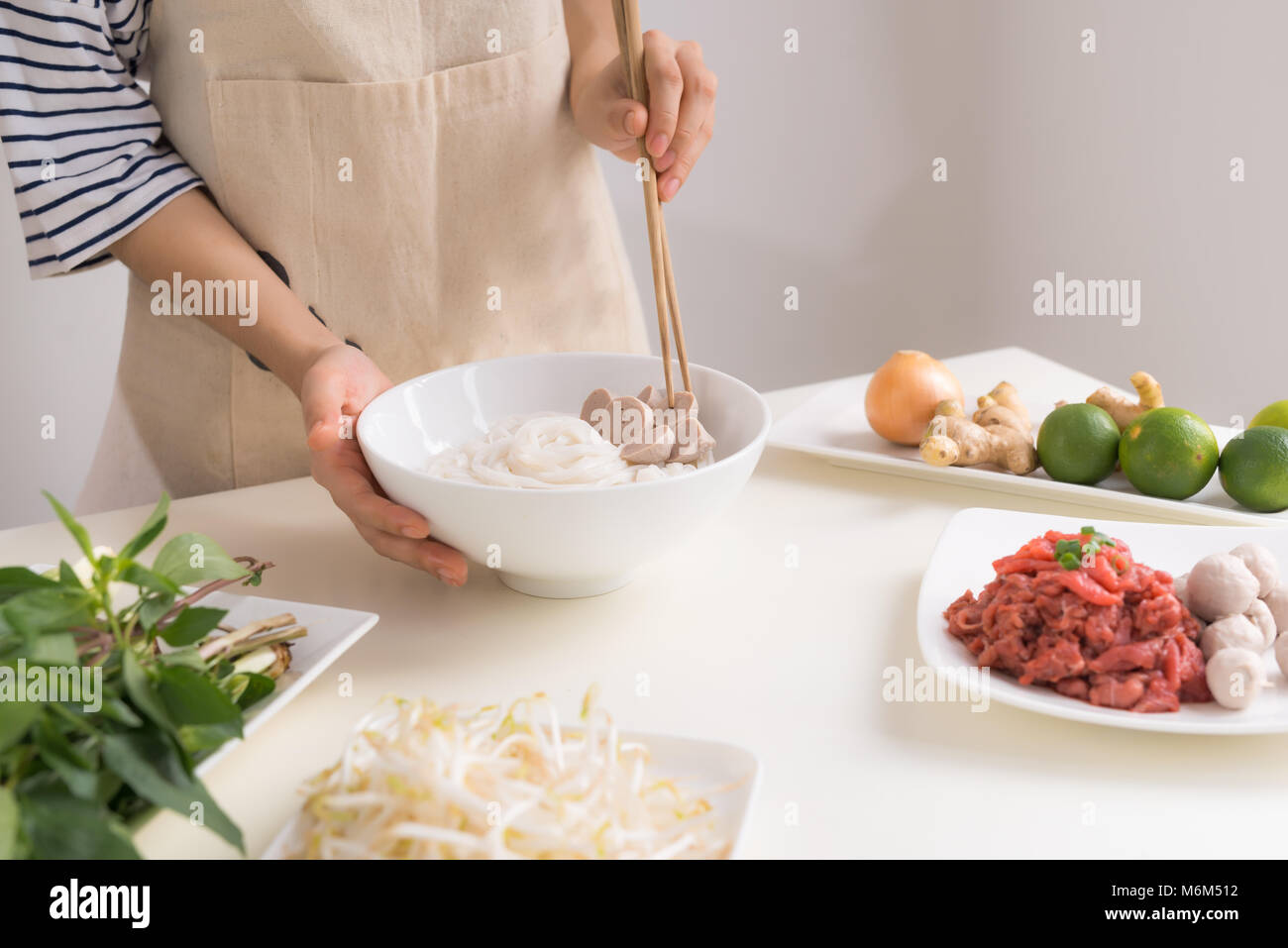 Female chef prepare traditional Vietnamese soup Pho bo with herbs, meat ...