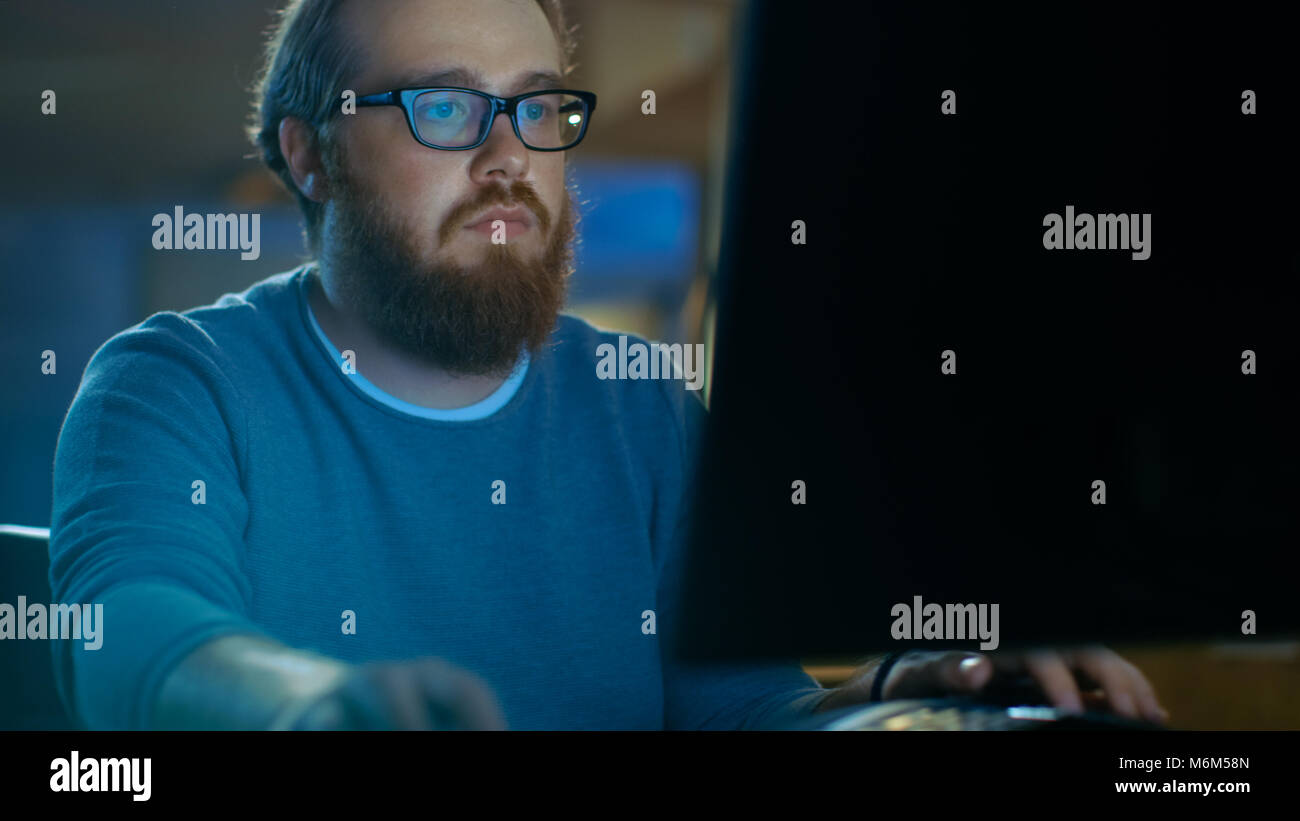 Focused Young Man Works on a Personal Computer. He Wears Glasses and Has Beard, He Works Late at ...