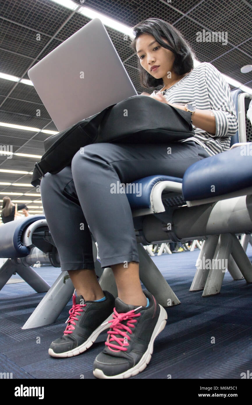 A young woman is working on a computer in an airport lobby while ...