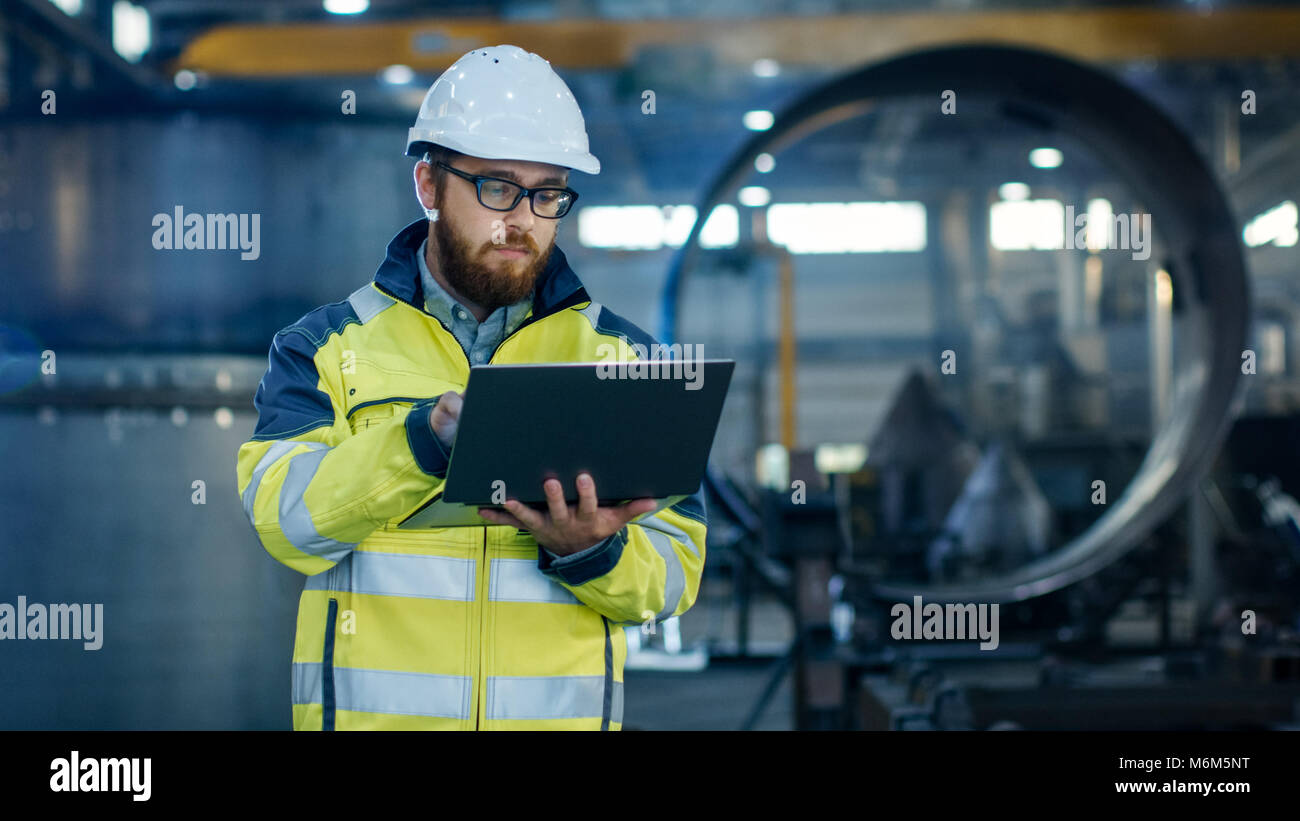Industrial Engineer in Hard Hat Wearing Safety Jacket Uses Laptop. He ...