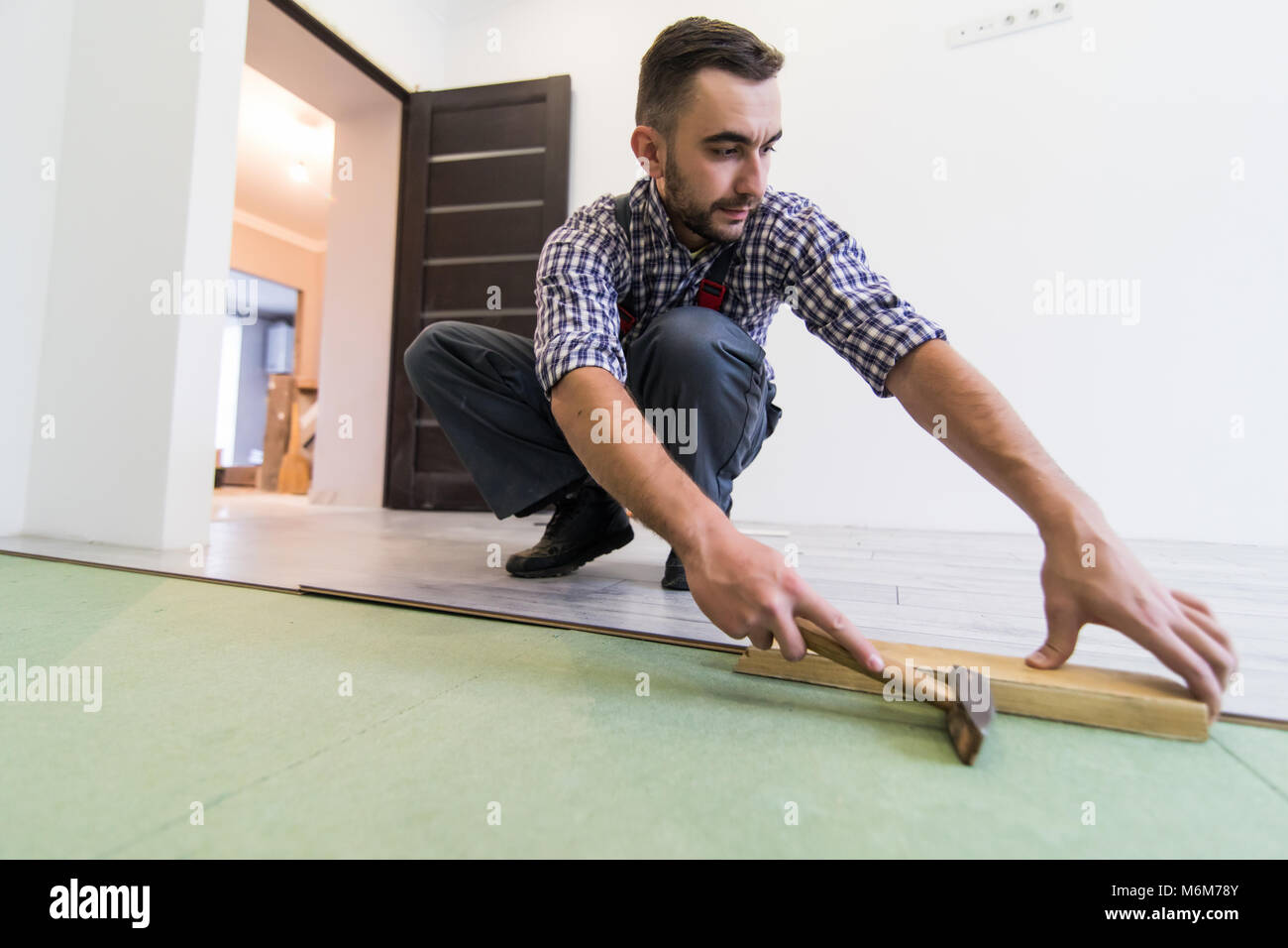Handsome man measuring wooden flooring with hammer install laminate ...