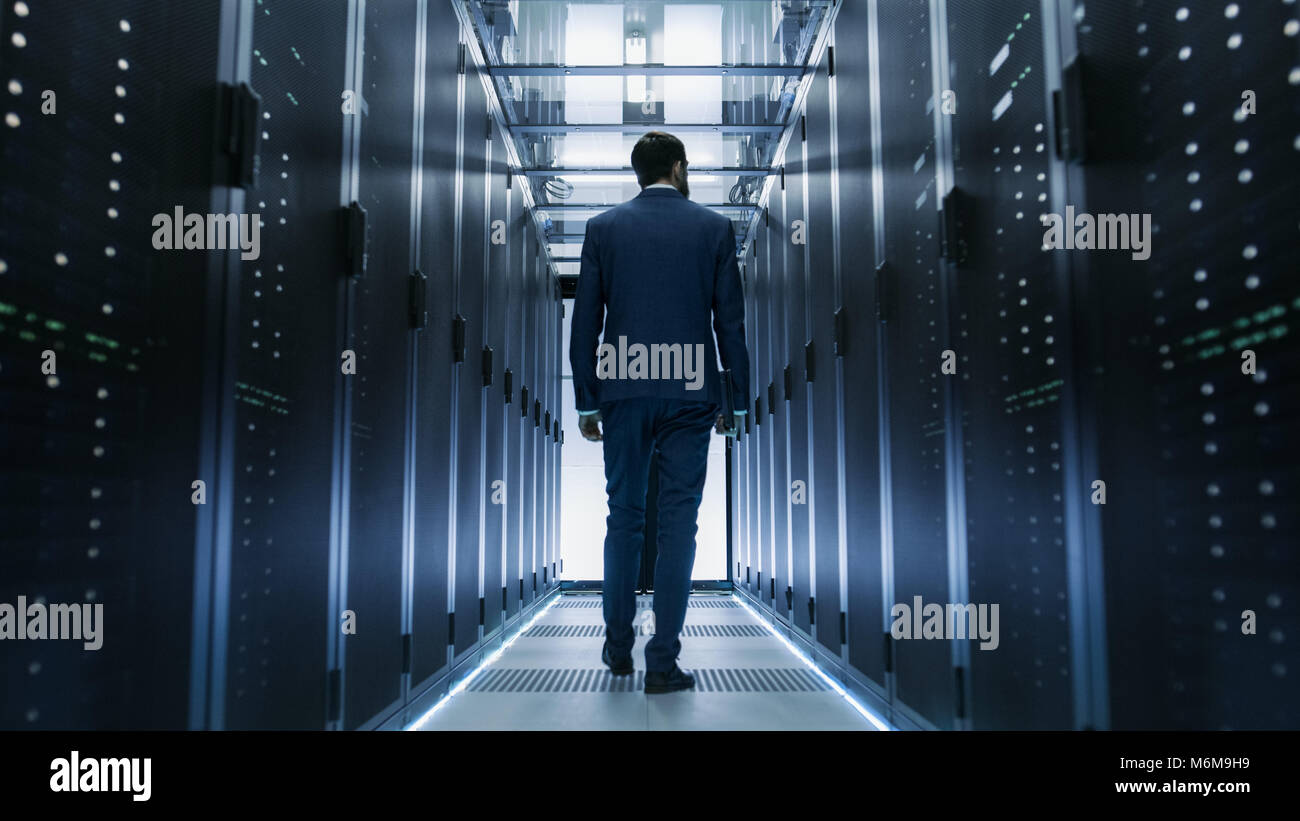 Following Shot of IT Engineer Walking Through Data Center with Rows of ...