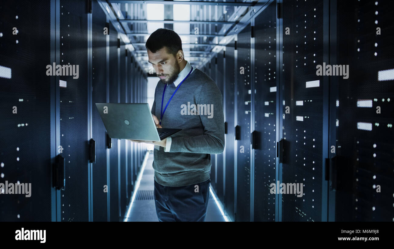 IT Technician Works on a Laptop in Big Data Center full of Rack Servers ...