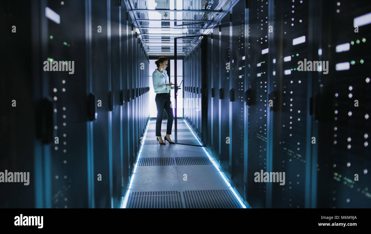 Female Server Technician Stands next to Cabinet in Data Center Corridor ...