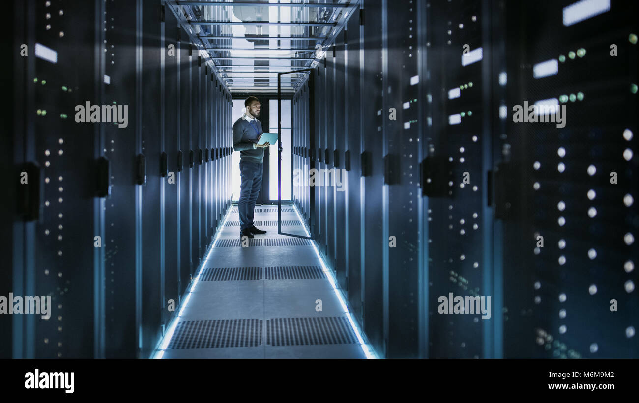 IT Technician Works on Laptop in Big Data Center full of Rack Servers ...