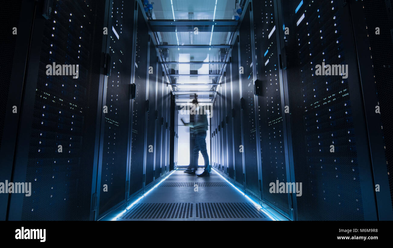 Male IT Engineer Walking and Working in Data Center Corridor. She is ...
