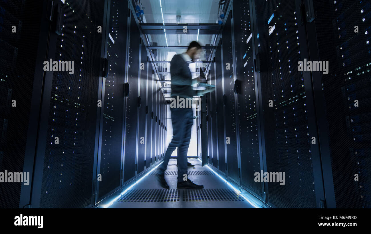 Male IT Engineer Walking and Working in Data Center Corridor. She is ...