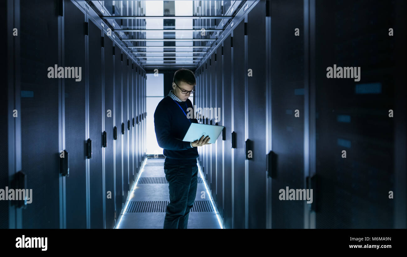 Male IT Engineer Works on a Laptop in front of Server Cabinet at a Big ...