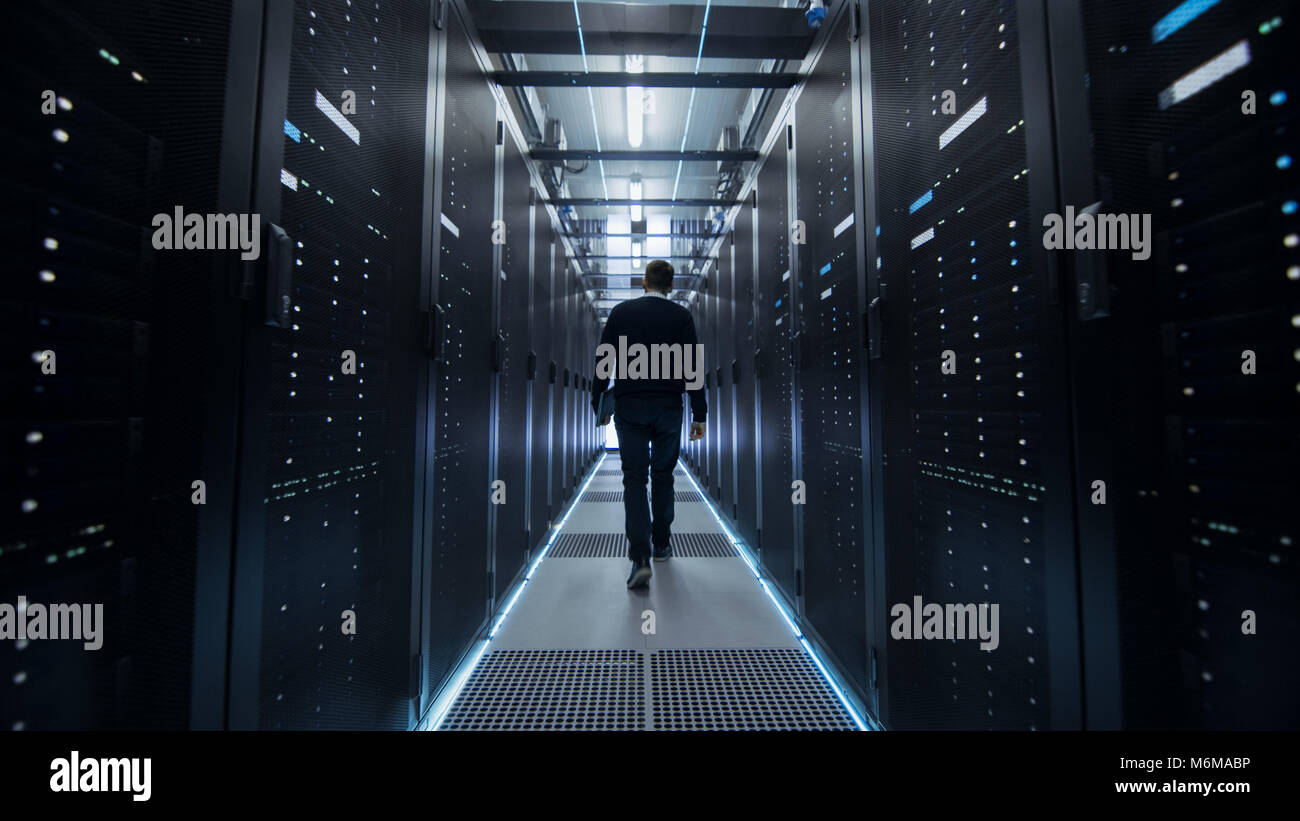 Following Shot of IT Engineer Walking Through Data Center Corridor with ...