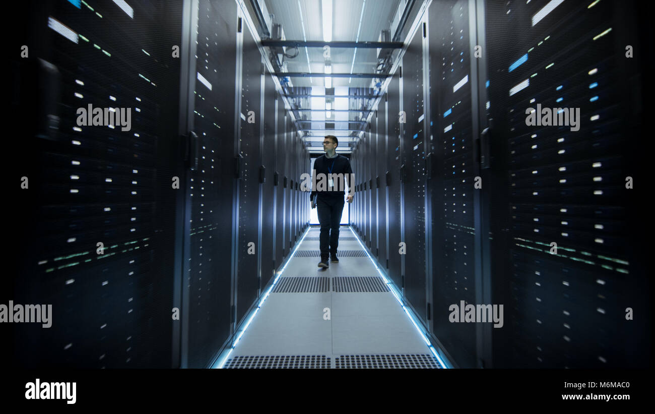 Shot of IT Engineer Walking Through Data Center Corridor with Rows of ...