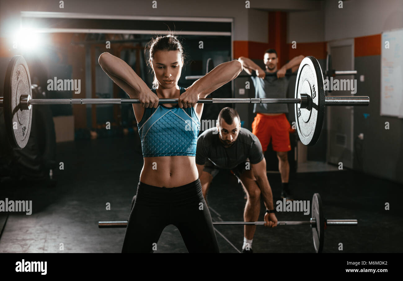 Young muscular cute woman doing exercise with barbell at the gym ...