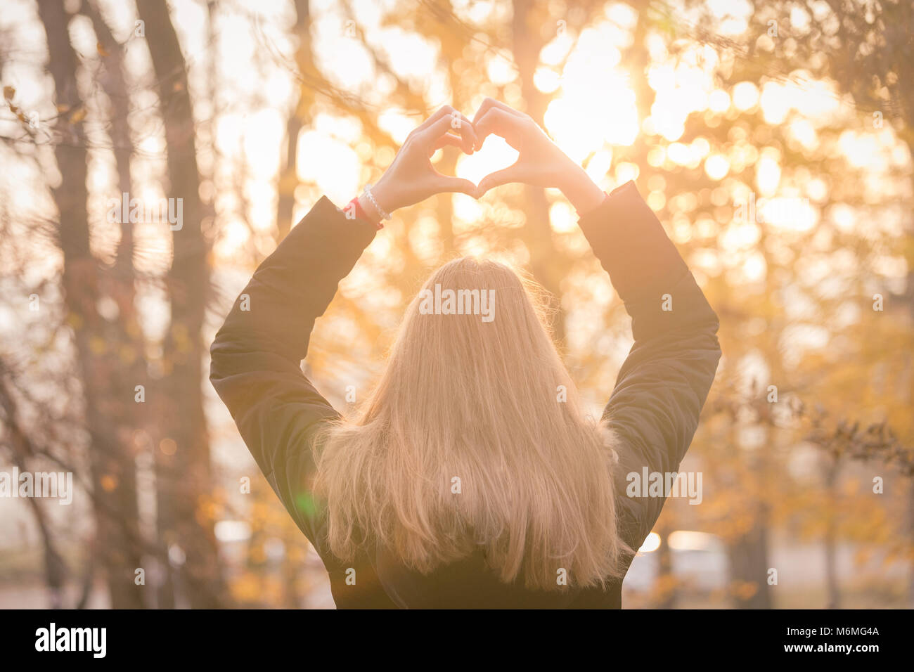 Rear view of female making heart shape with her hands in the woods ...